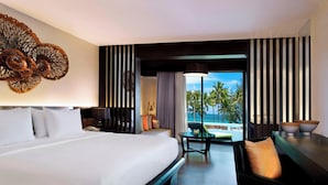 Quarto de hotel com cama grande, uma escrivaninha, uma cadeira, vista para o mar e um objeto decorativo na parede.
