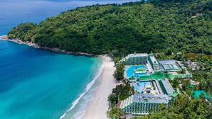 Vista aérea de um resort com praia, área de piscina e vegetação exuberante.