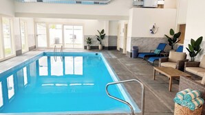 Piscina interna com água cristalina, rodeada por espregui çadeiras e um sofá de vime.