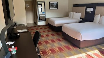Quarto de hotel com duas camas, uma escrivaninha com cadeira, televisão e carpete estampado.