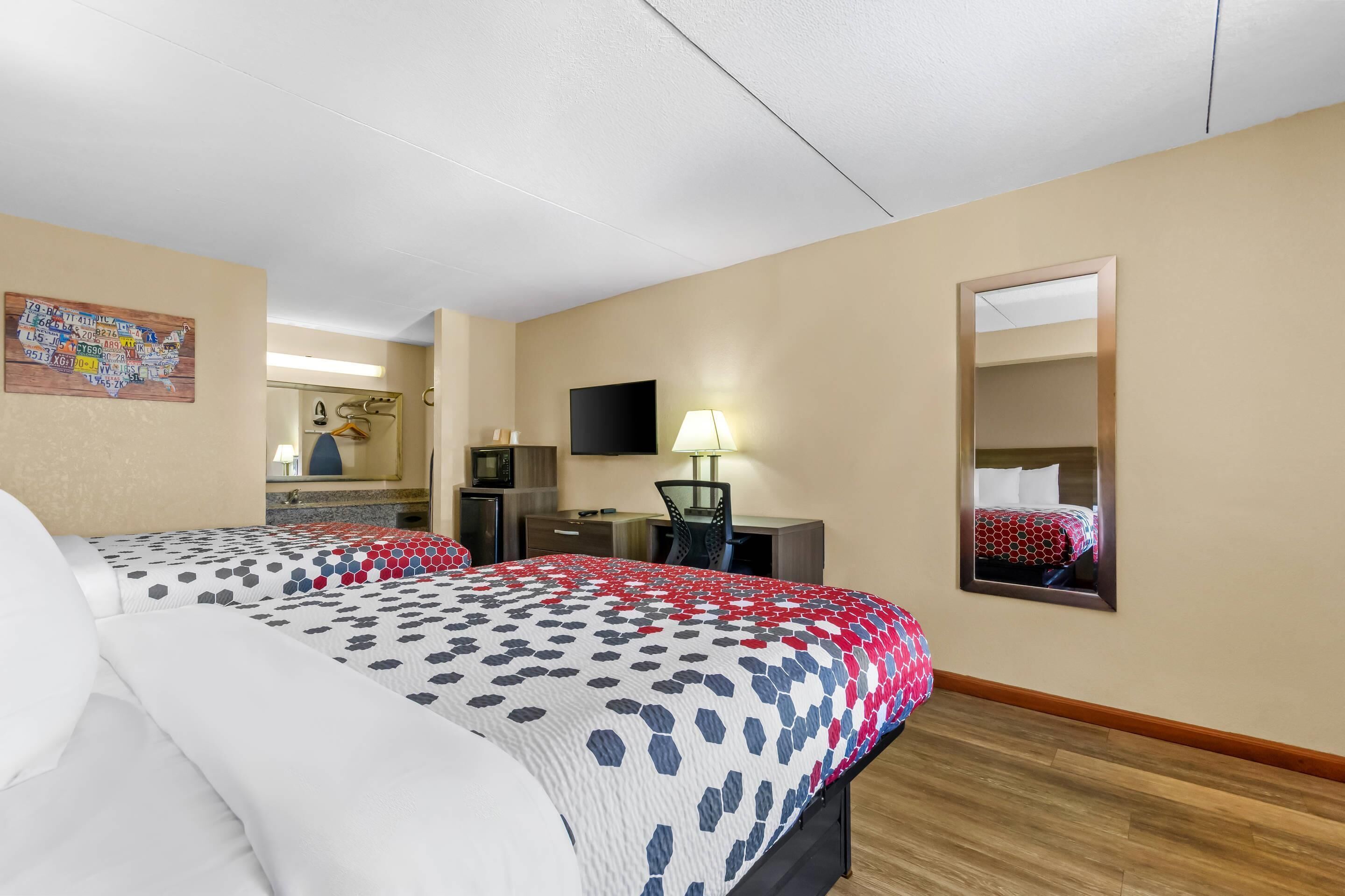 Quarto de hotel com uma cama grande, uma escrivaninha, uma cadeira, uma televisão e um espelho.