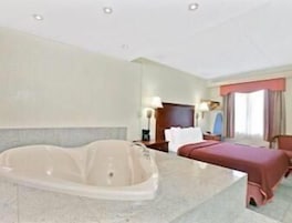 Quarto de hotel com uma banheira grande, uma cama, uma escrivaninha e uma janela com cortinas.