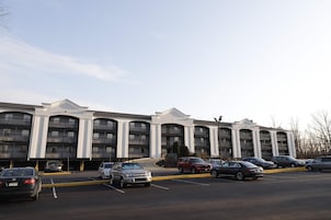 Um hotel com vários andares, fachada simétrica, diversas varandas e um estacionamento com vários carros.