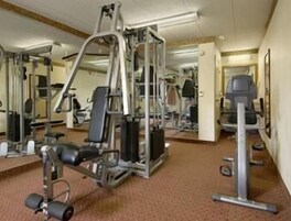 Uma academia com diversos equipamentos de exercício, espelhos e pesos.