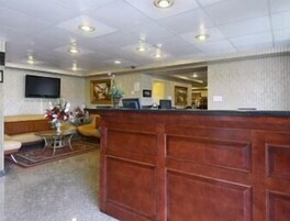 Um saguão de hotel com balcão de recepção, área de estar e uma televisão na parede.