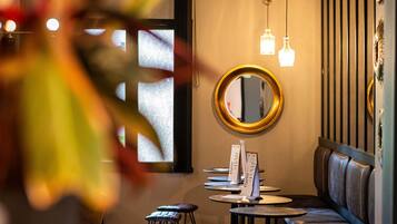 Interior de restaurante com um espaço de assentos em bancos compridos, mesas redondas, luminárias pendentes e um espelho fixado na parede.
