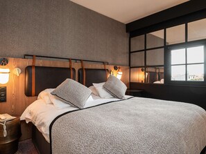 Quarto de hotel com cama grande, luminárias de cabeceira, mesa de apoio, telefone e janela com vista.