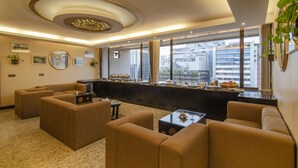 Um hall de hotel moderno com área de bar, assentos confortáveis e grandes janelas com vista para a cidade.