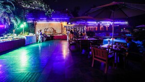 Uma área de refeições ao ar livre com mesas, cadeiras, um bar e uma piscina.