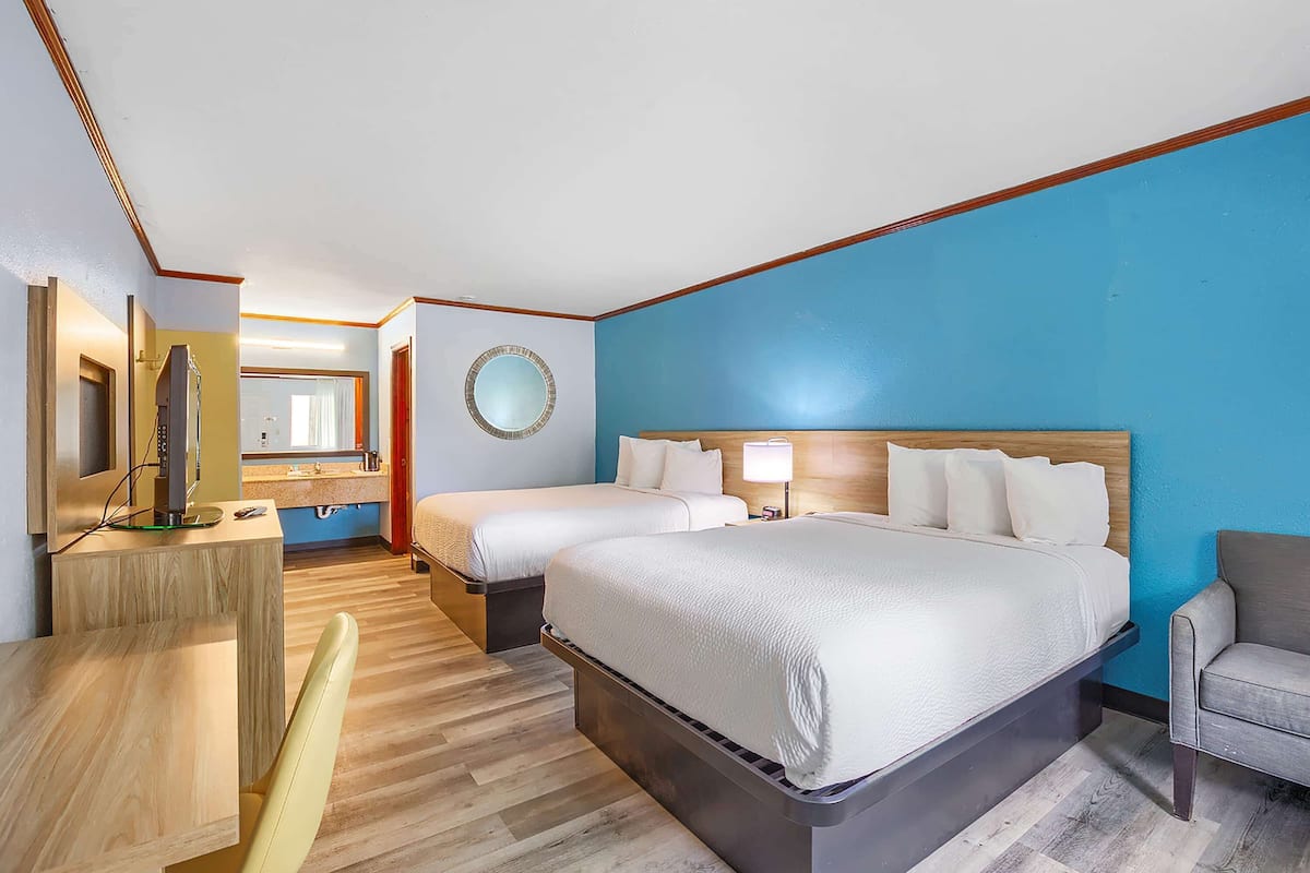 Quarto de hotel com duas camas, uma escrivaninha, uma cadeira, um espelho e uma televisão.