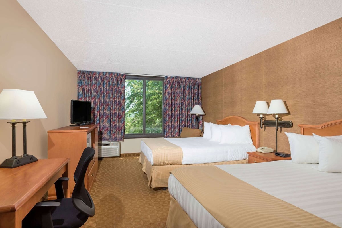 Quarto de hotel com cama, escrivaninha, cadeira, televisão e duas luminárias.