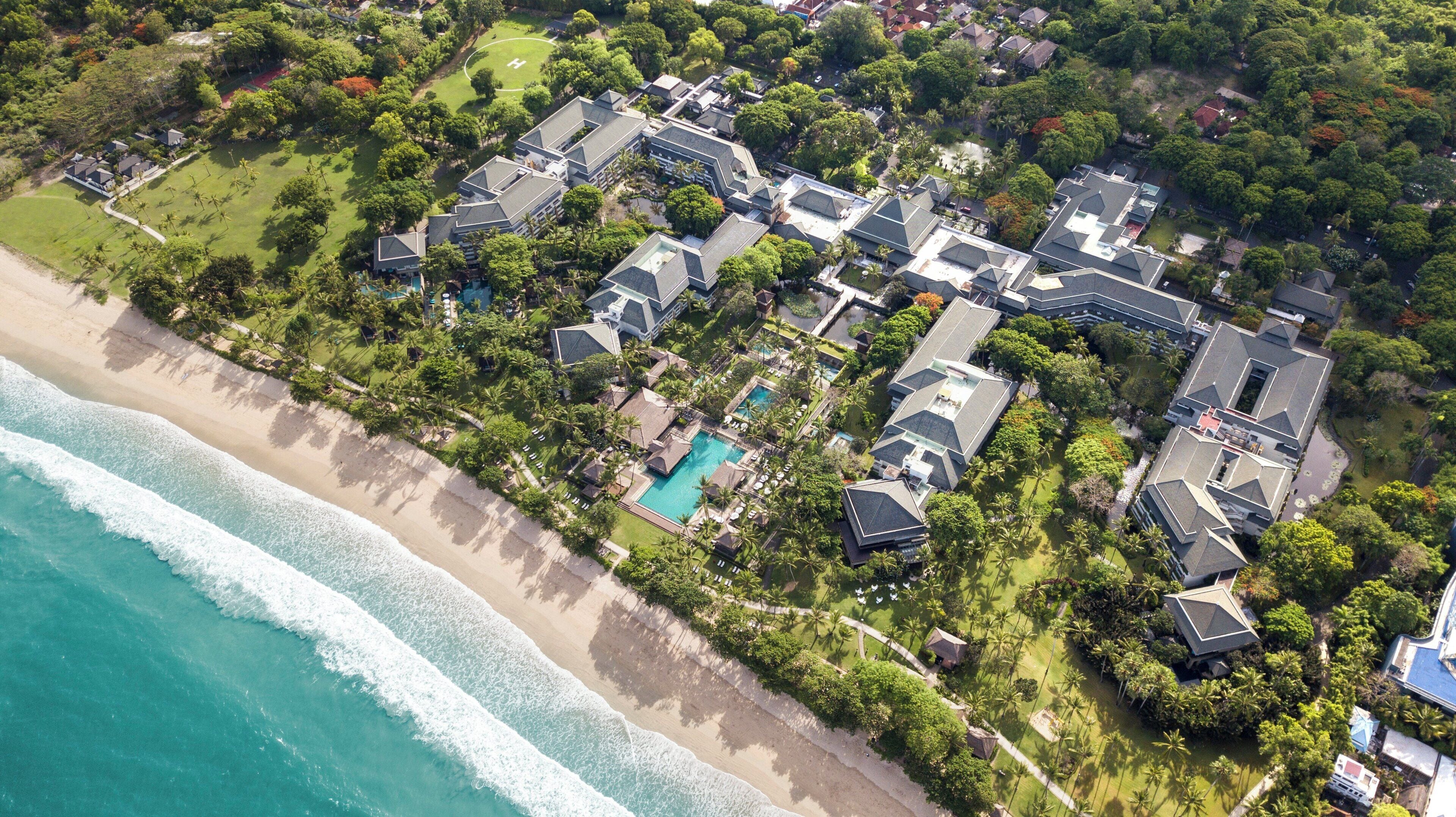 Vista aérea de um resort costeiro com vários edifícios, piscina e praia.