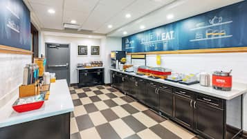 Uma cozinha moderna com piso xadrez, balcão com diversos alimentos e parede de lousa com desenhos relacionados à culinária.