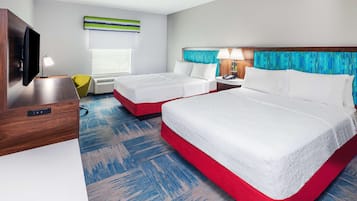 Quarto de hotel com duas camas, uma mesa de escritório, uma televisão de tela plana, uma cadeira e uma janela com cortinas.