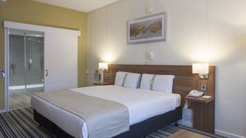 Quarto de hotel com uma cama grande, luminárias de cabeceira, um telefone e um quadro na parede.