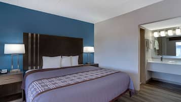Quarto de hotel com cama grande, abajures, mesa de cabeceira e banheiro com pia e espelho.