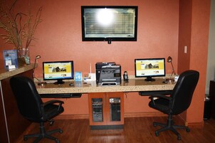 Uma mesa de recepção com dois monitores de computador, uma impressora e duas cadeiras de escritório.