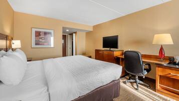 Quarto de hotel com uma cama grande, uma mesa de trabalho com computador, televisão e luminária.