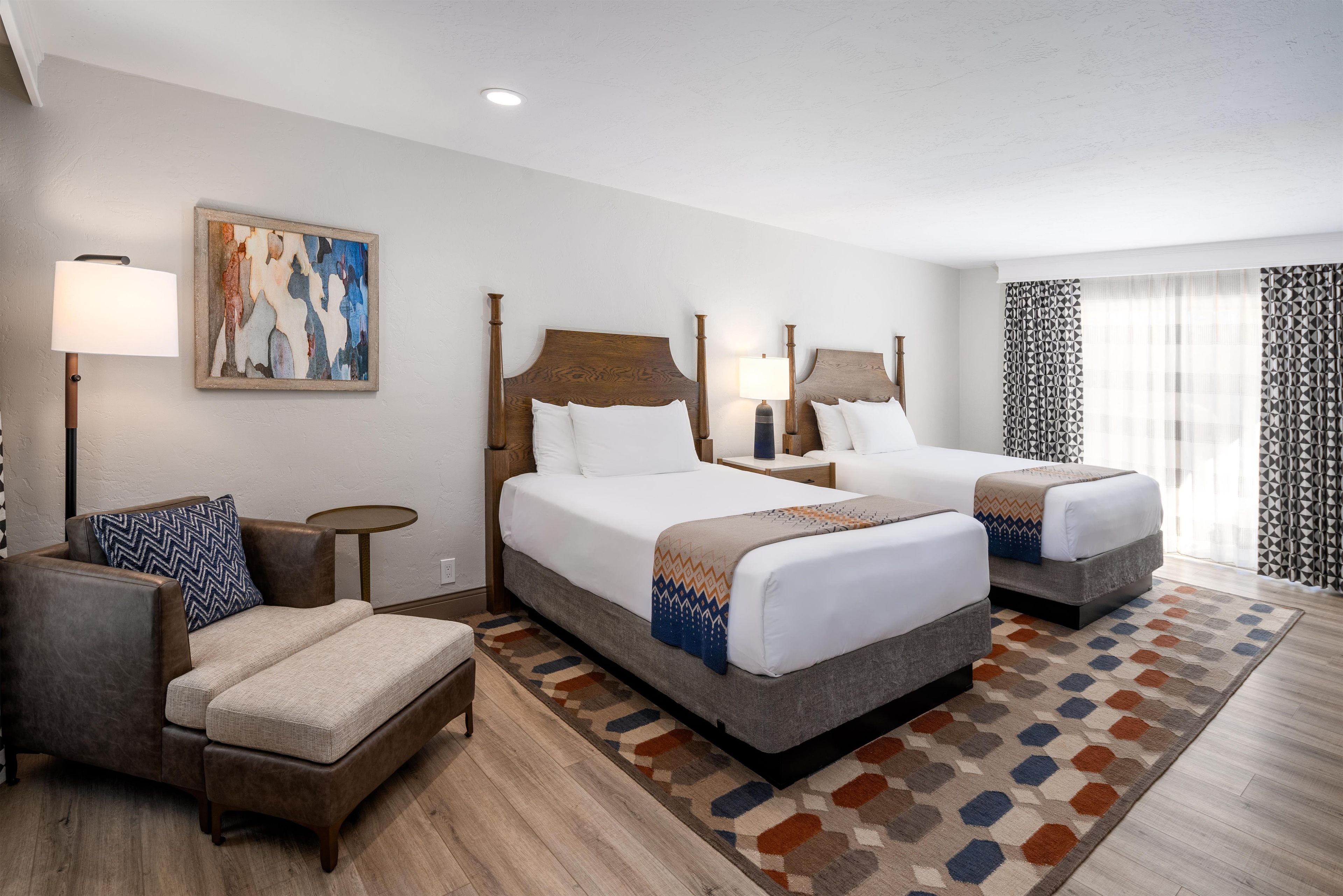 Quarto de hotel com duas camas, um sofá, uma mesinha e um quadro na parede.