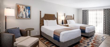 Quarto de hotel com duas camas, um sofá, uma mesinha e um quadro na parede.