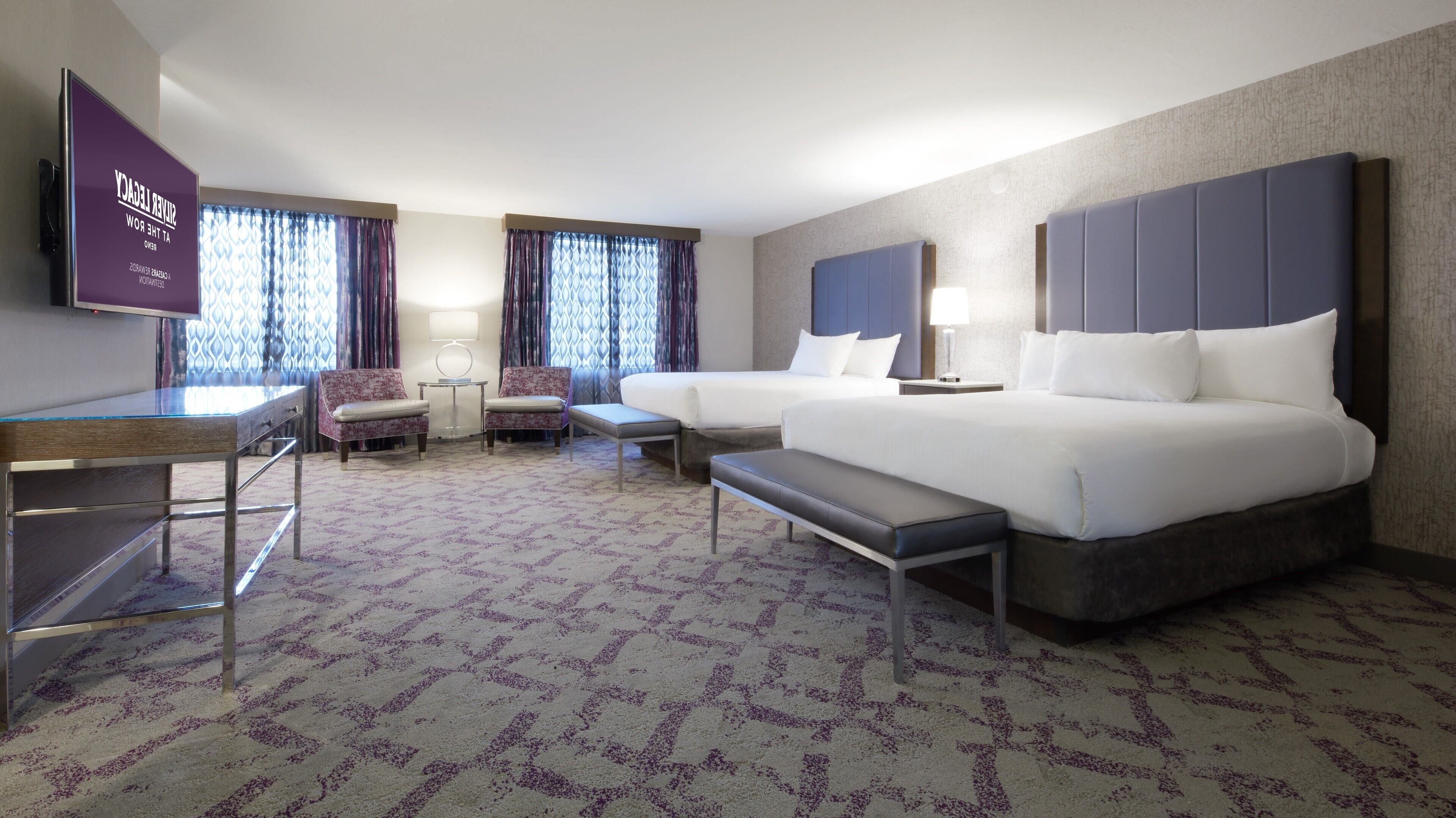 Quarto de hotel com uma cama, duas poltronas, uma escrivaninha e uma televisão.