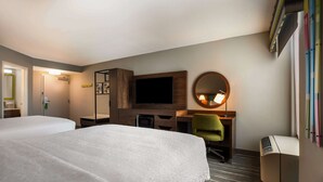 Quarto de hotel com duas camas, uma escrivaninha, televisão de tela plana, um espelho e um pequeno aquecedor.