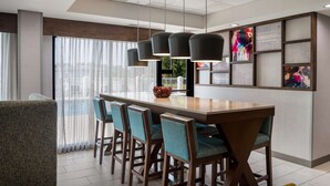 Uma área de jantar moderna com uma grande mesa de madeira, quatro cadeiras e luminárias pendentes.