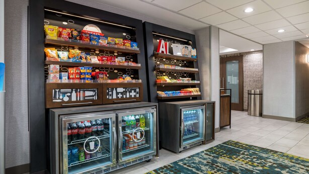 Uma área de autoatendimento com lanches e bebidas, incluindo Coca-Cola e outras opções, e um letreiro com a frase 'Sweet Home'.