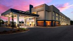 Um hotel Hampton Inn com design moderno, apresentando uma entrada bem iluminada e uma área de estacionamento coberta.