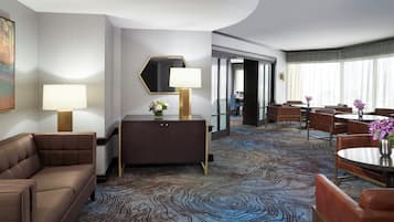 Quarto de hotel com sofá, mesa de escritório com luminária, espelho e área de jantar com cadeiras e mesa.