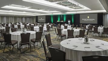 Uma sala de conferências com várias mesas redondas, cadeiras e um palco com uma tela.