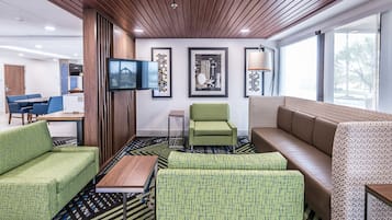 Um saguão moderno de hotel com teto de madeira, sofás estampados em verde, um sofá de couro marrom e obras de arte emolduradas nas paredes.