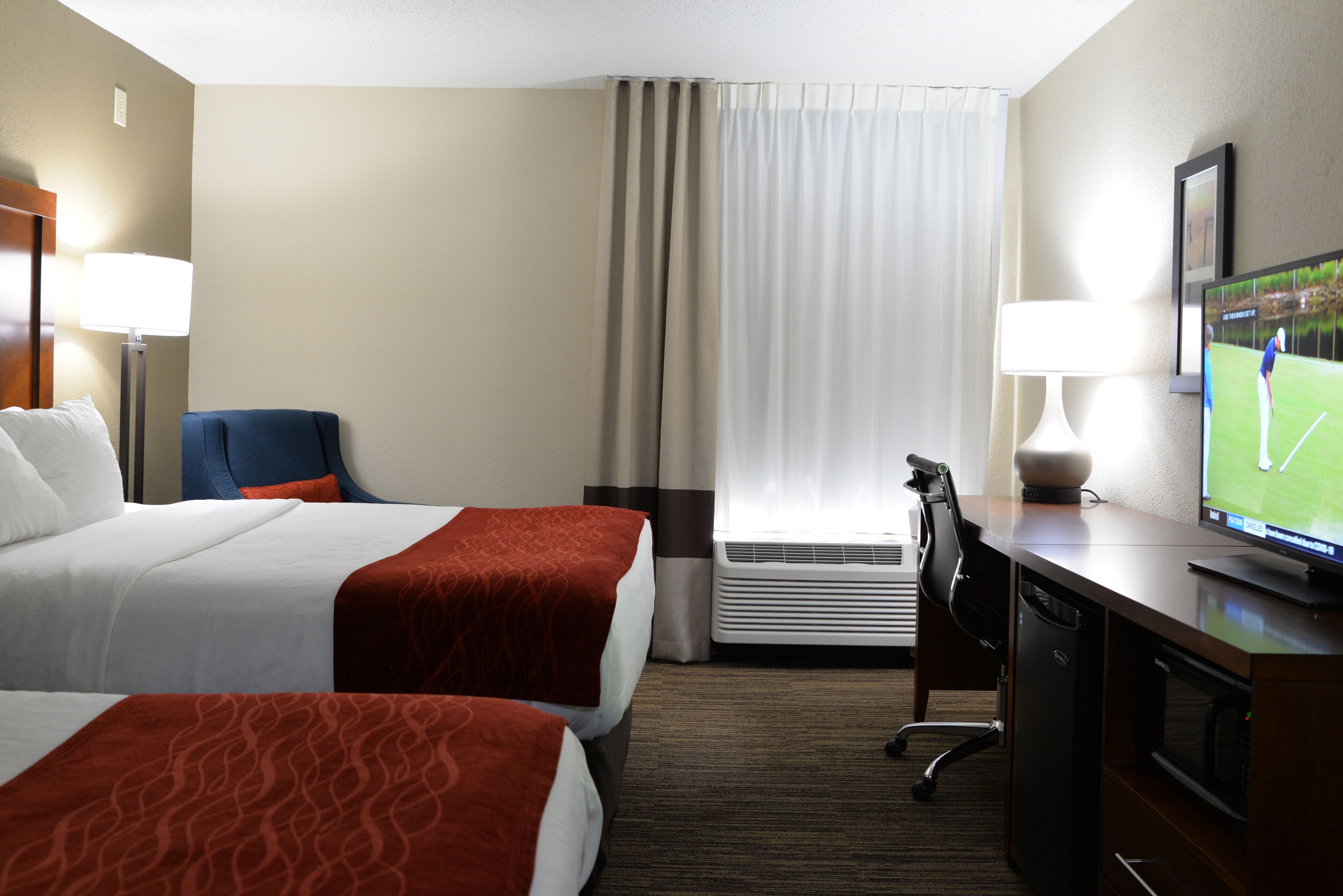 Quarto de hotel com duas camas, uma escrivaninha com televisão, uma cadeira e um ar condicionado.