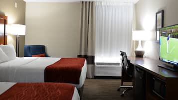 Quarto de hotel com duas camas, uma escrivaninha com televisão, uma cadeira e um ar condicionado.