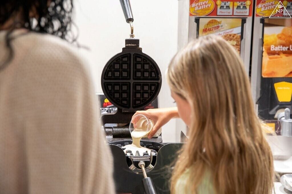 Uma máquina de waffles com alguém despejando massa nela.