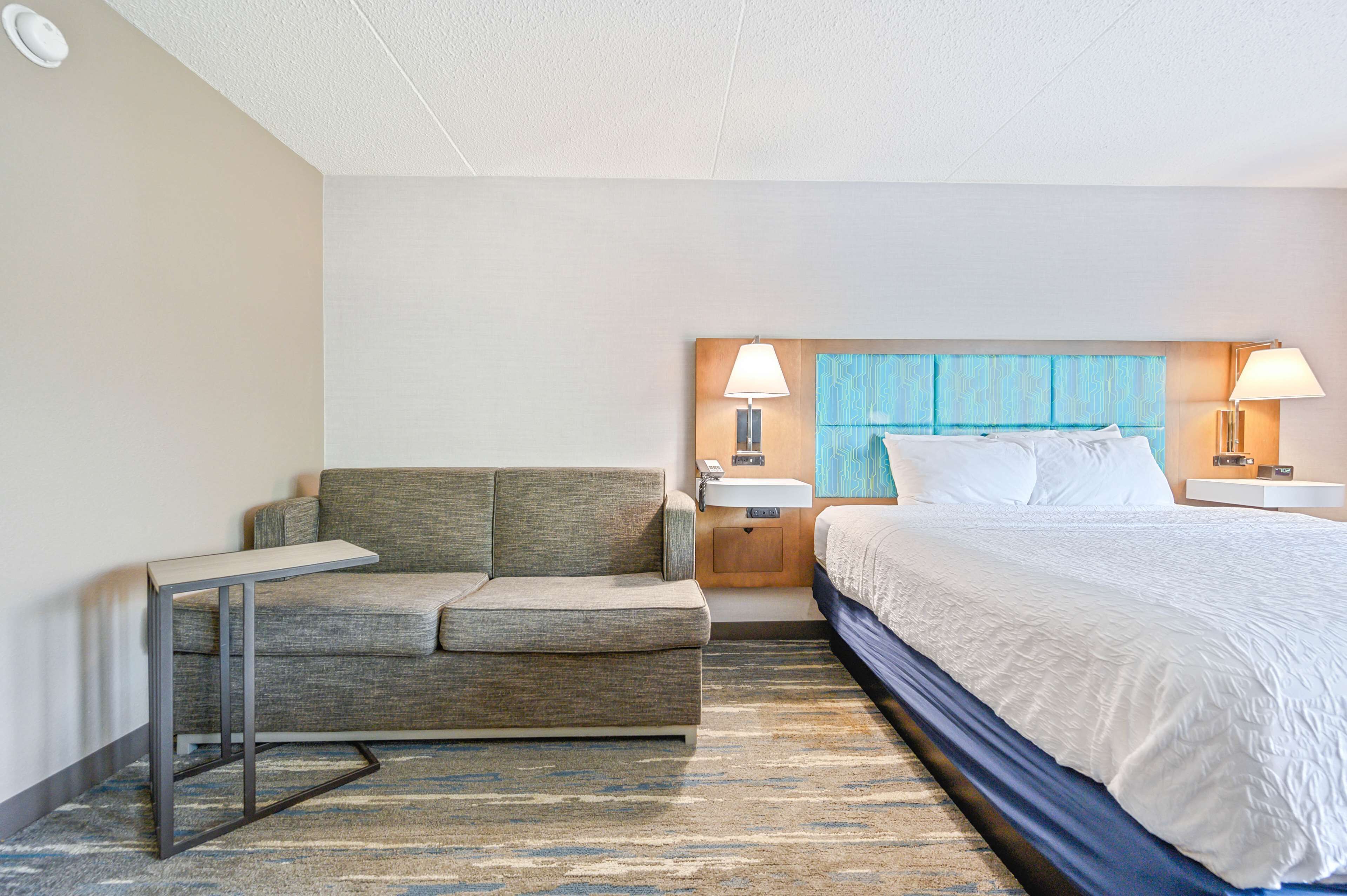 Quarto de hotel com cama, sofá, mesa de cabeceira e abajur.