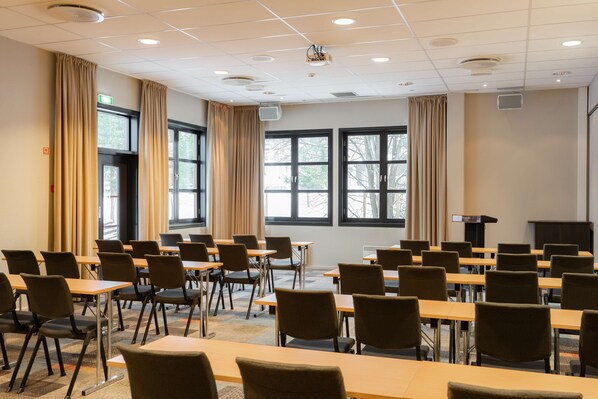 Uma sala de conferências com várias mesas e cadeiras, janelas amplas e um pódio.