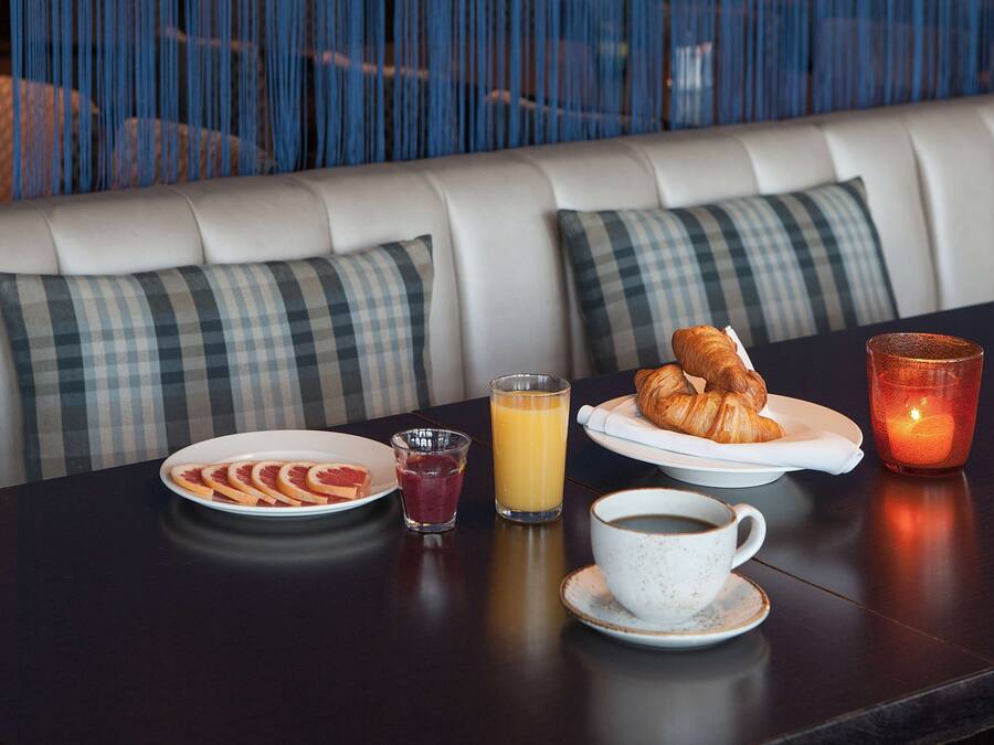 Uma mesa posta para o café da manhã, com croissants, um copo de suco de laranja, uma xícara de café e uma vela.