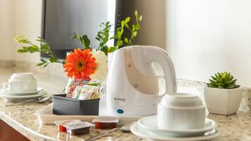 Uma kitchenette de hotel com cafeteira, chaleira e um pequeno vaso de planta.
