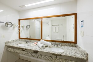 Casa de banho com duas pias, um espelho grande e um secador de cabelo fixado na parede.
