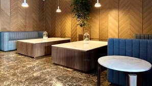Um lobby moderno com parede de madeira em padrão herringbone, duas áreas de estar com bancos estofados em azul e piso de mármore.