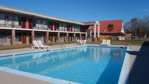 Um hotel com piscina, área de estar externa e um edifício com telhado vermelho.