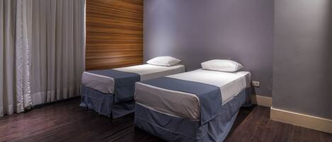 Quarto de hotel com duas camas de solteiro, painéis de madeira em uma parede e piso de madeira escura.