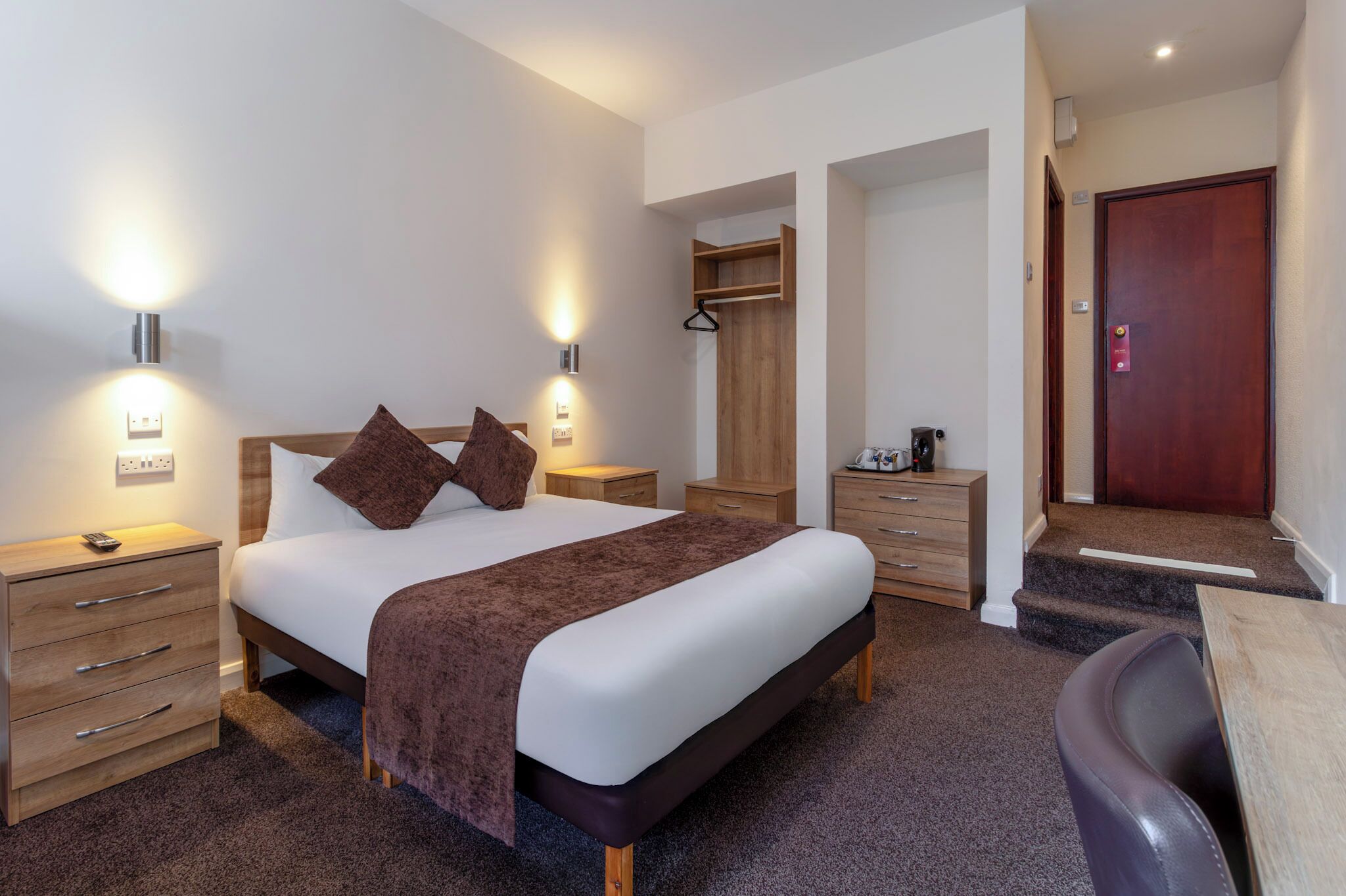 Quarto de hotel bem arrumado com uma cama grande, mesas de cabeceira, guarda-roupa e escrivaninha com cadeira.
