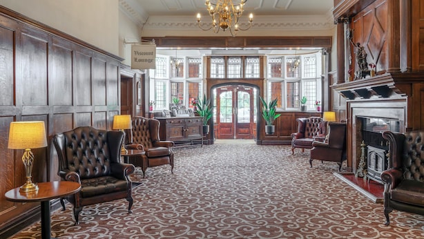 Um hall imponente com carpete estampado, poltronas de couro, um lustre e uma lareira.