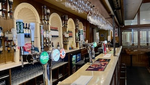 Uma área de bar com várias torneiras de cerveja, um balcão e prateleiras com diversos tipos de garrafas.