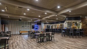 Uma área de bar com balcão, banquetas e mesa de bilhar.