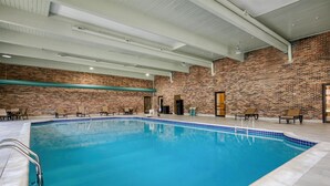 Uma piscina interna com parede de tijolos, cadeiras de descanso e piso revestido de azulejos.