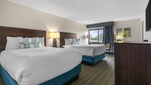 Quarto de hotel com duas camas, uma escrivaninha e uma janela grande.