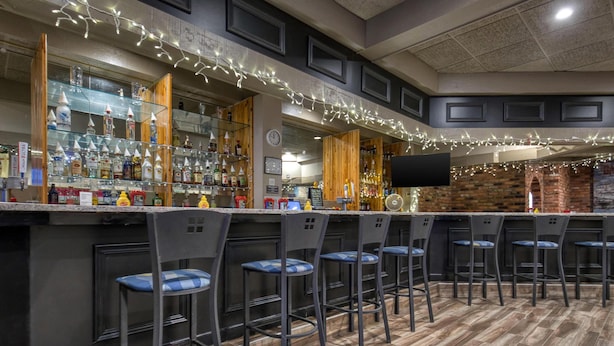 Uma área de bar com balcões de madeira, vários bancos e um painel de parede de tijolos.